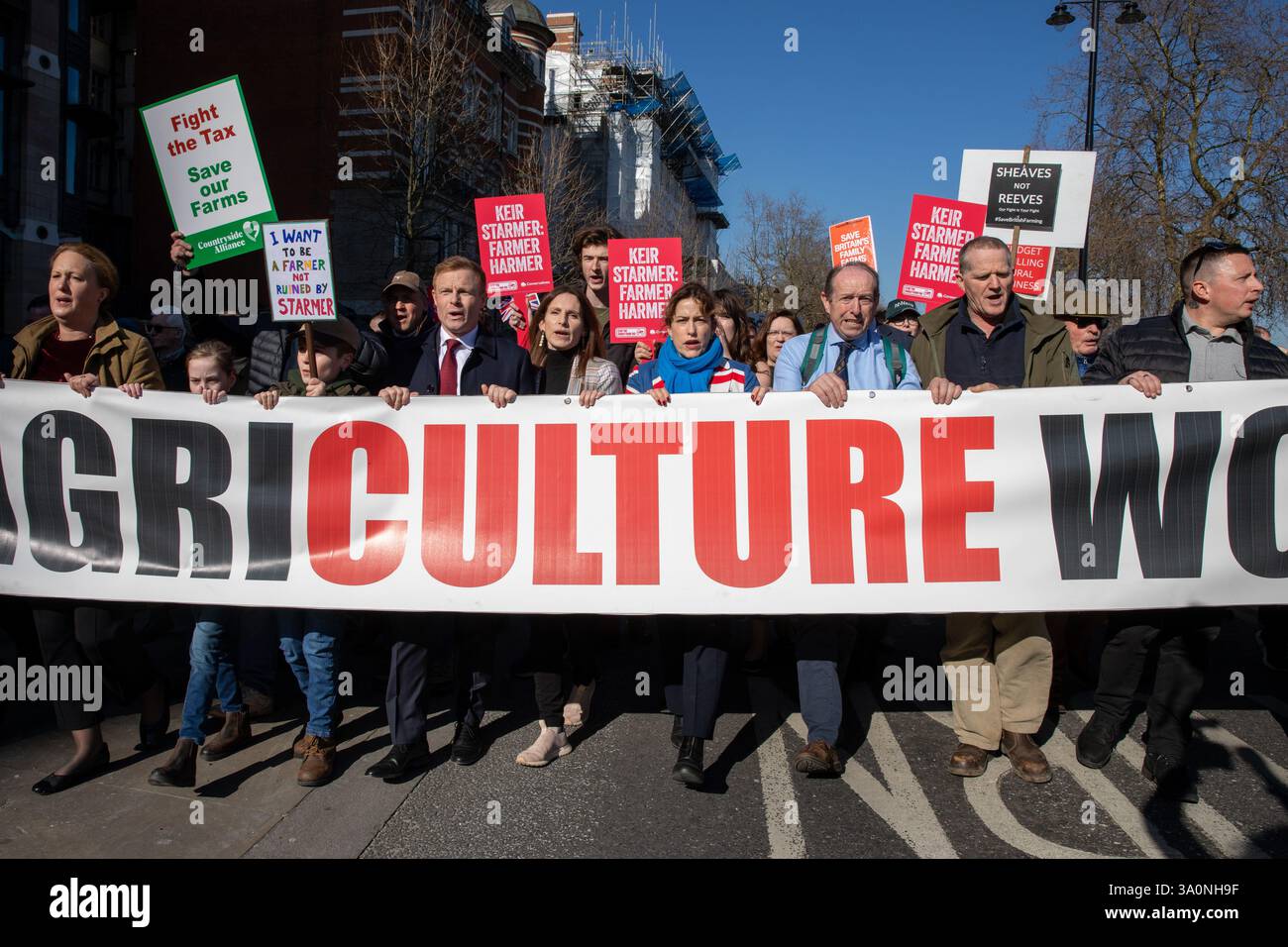Protesters march behind a protest banner with placards expressing their ...