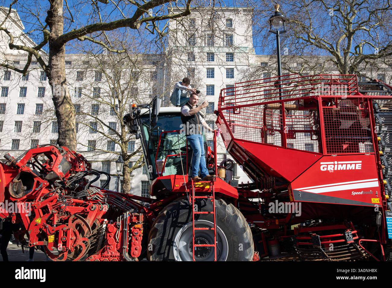 Two protesters stand atop of a farming tractor to take photographs with ...