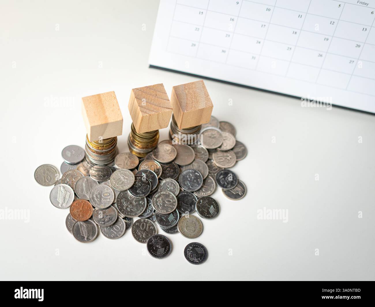 3 wooden blocks on top of stacked coins, next to table calendar. High ...
