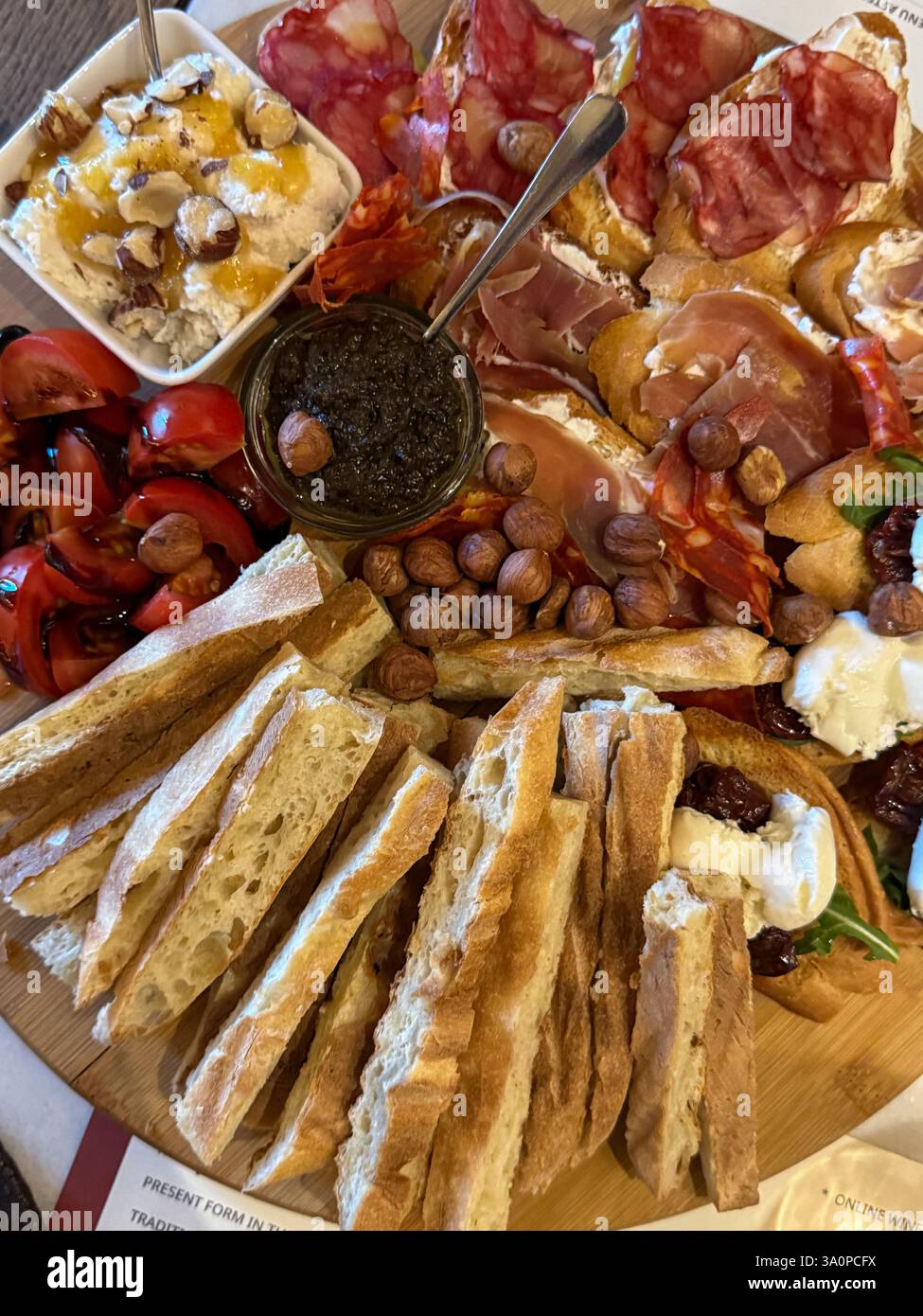 A wooden charcuterie board featuring sliced bread, cheeses, cured meats ...