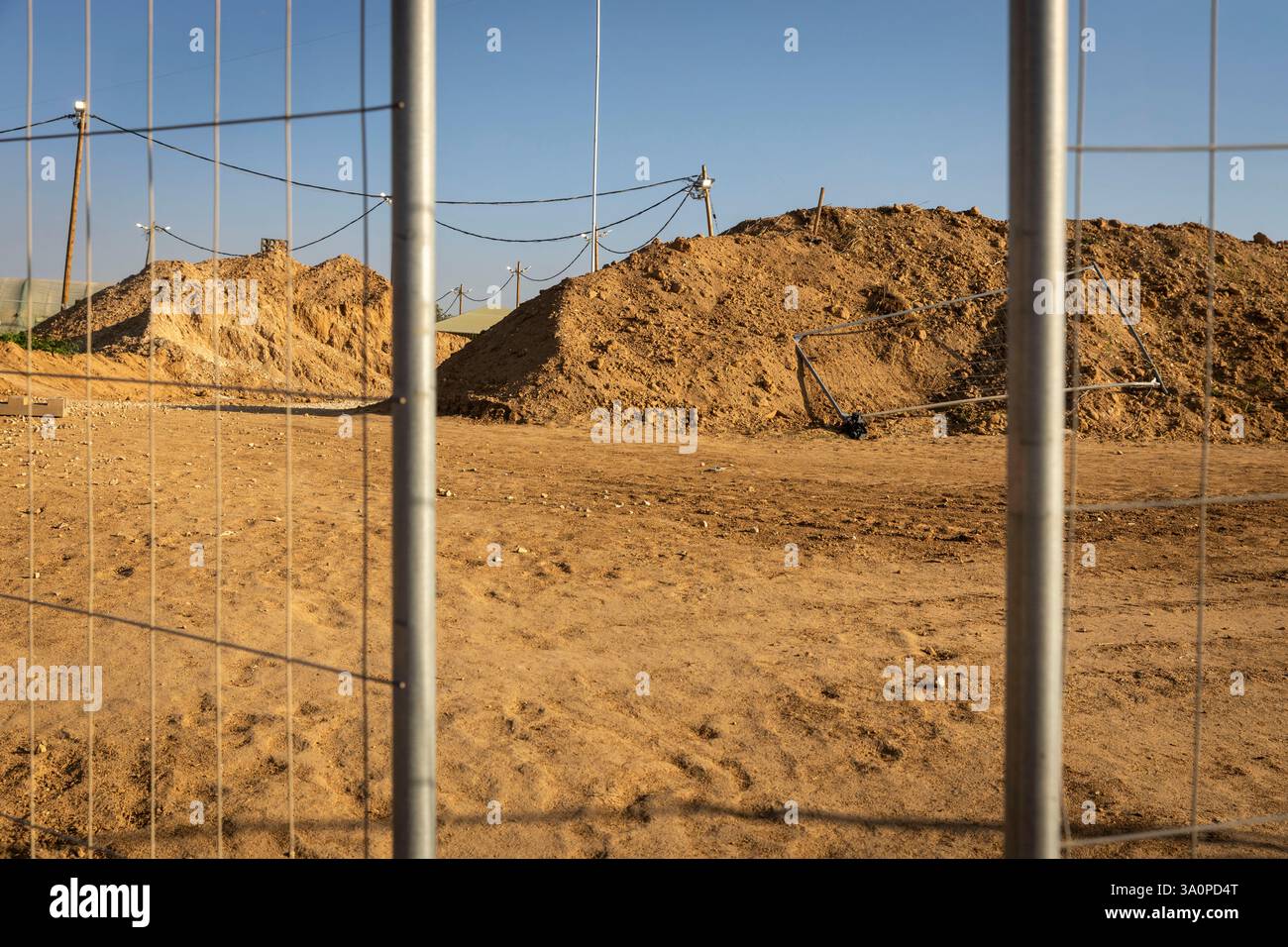 Fenced area with sand mounds and damaged structures in a conflict zone ...