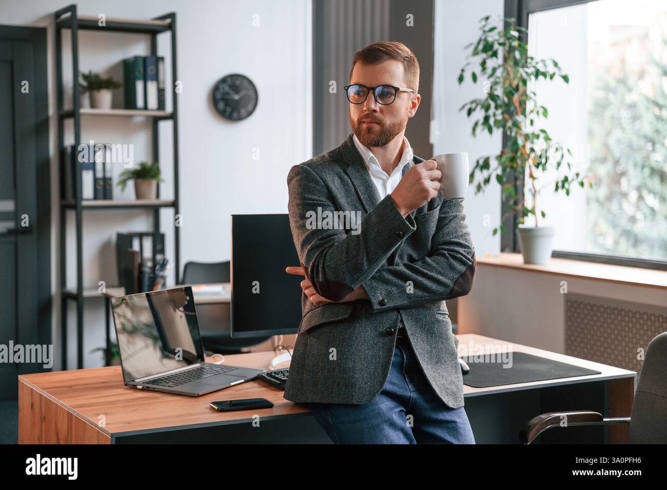 Leaning on the table. Businessman in suit is in the office with ...