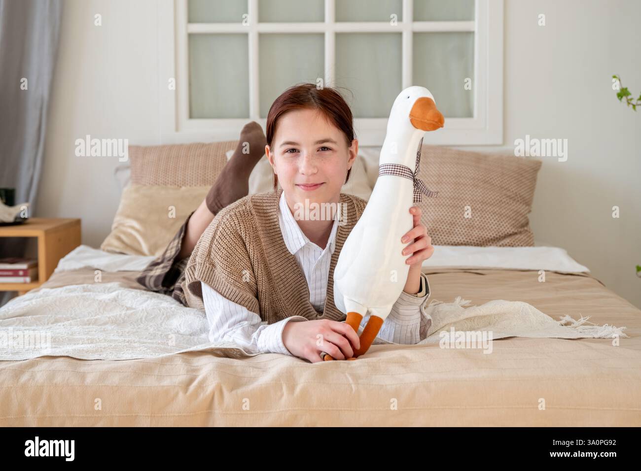 Preteen girl wearing a sweater and a white shirt is lying on her bed ...