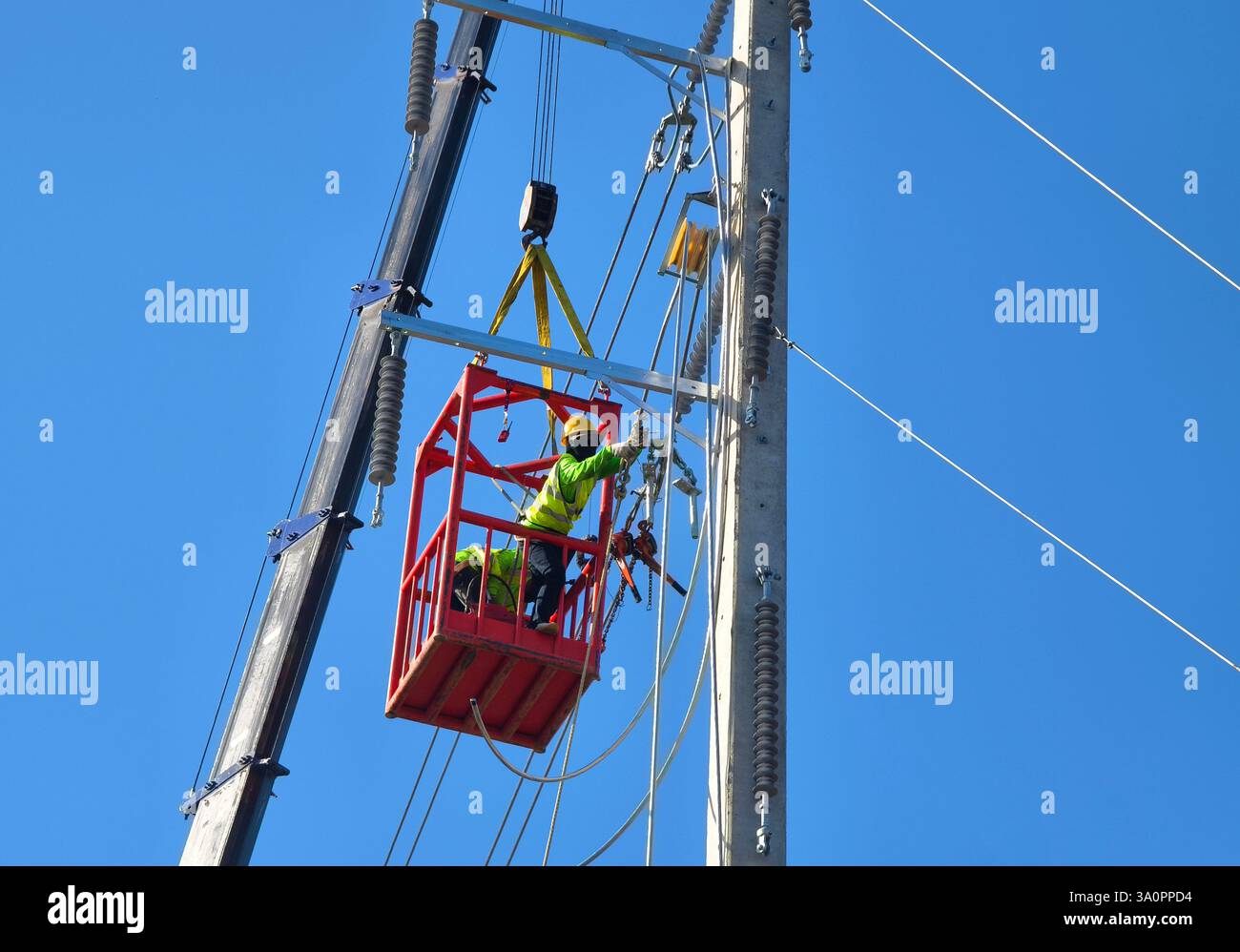 Men in work clothes and hard hats are installing high-voltage wires on ...