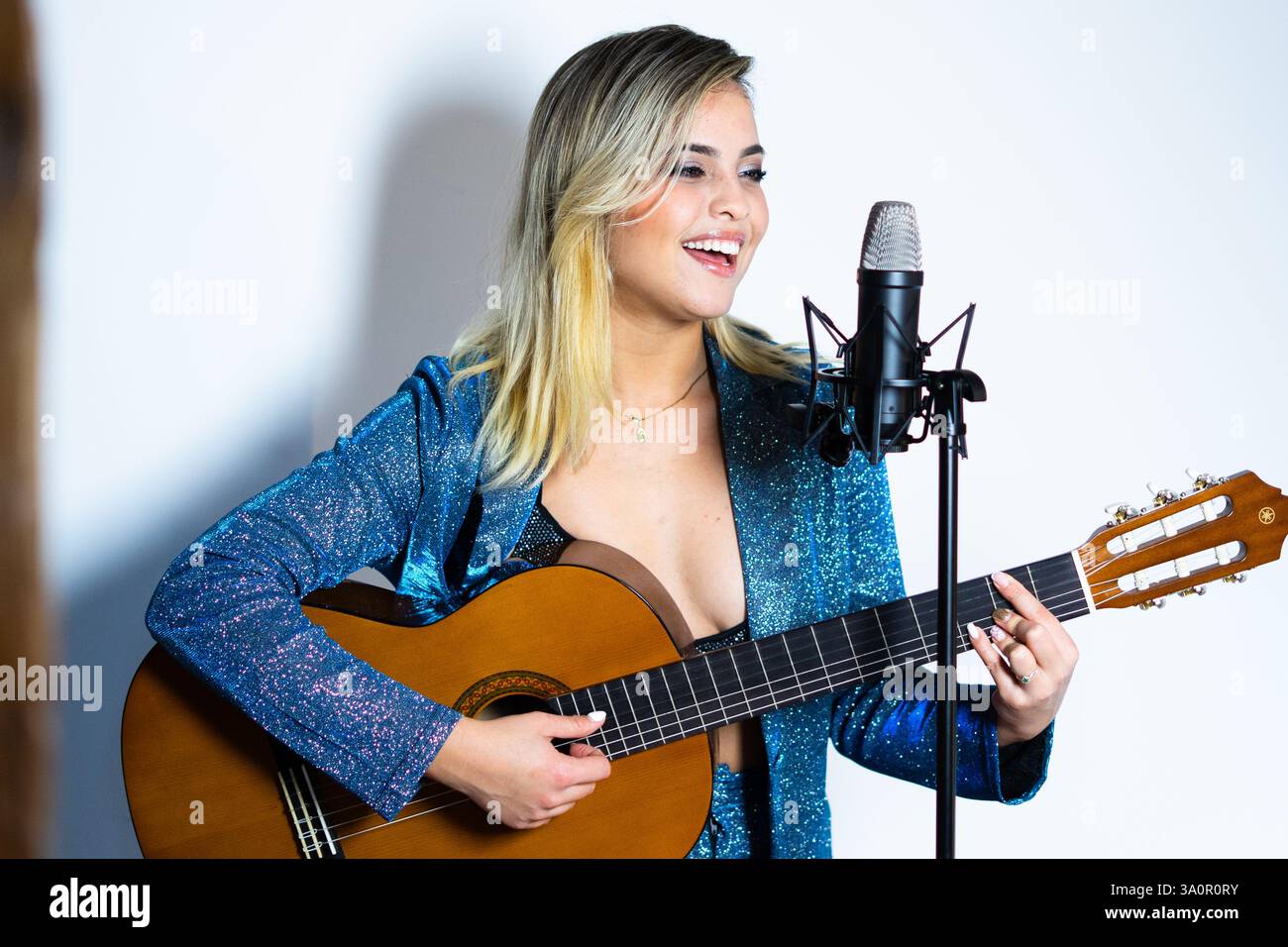 Female musician recording a song, playing acoustic guitar and singing ...