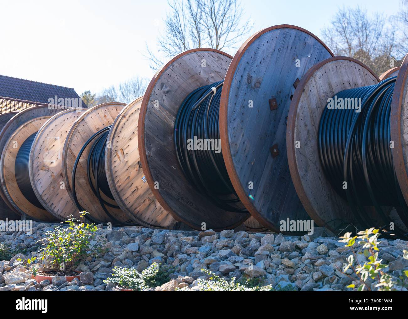 Wooden cable drums with black wire are stored in an open warehouse ...
