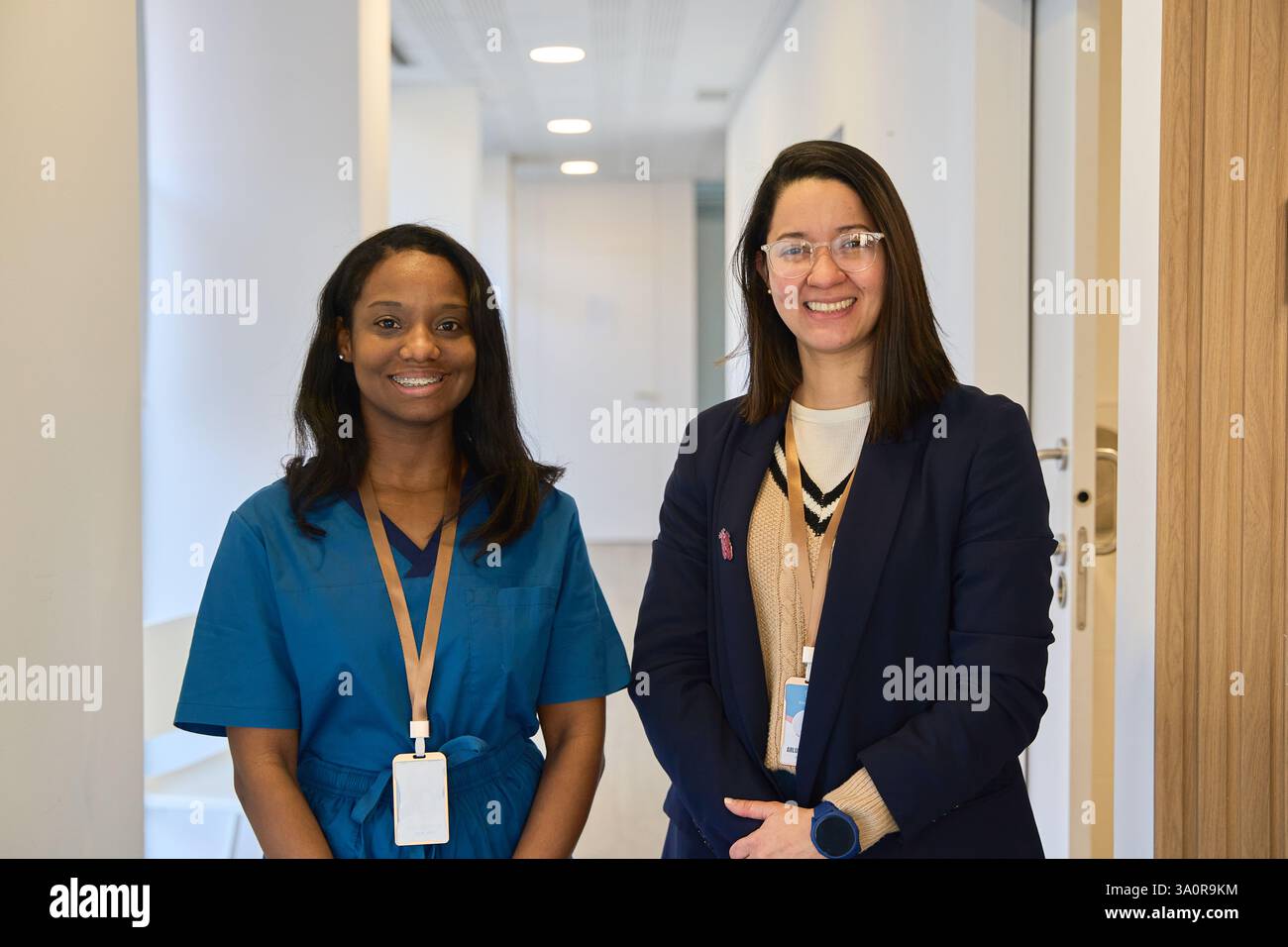 Two female doctors smiling in a bright, modern hospital corridor ...