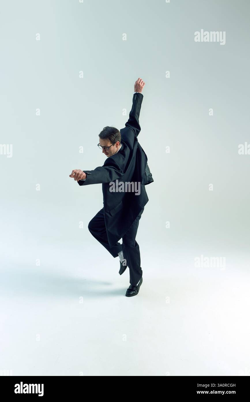 Businessman balancing on one foot with arm raised, suit moving with ...