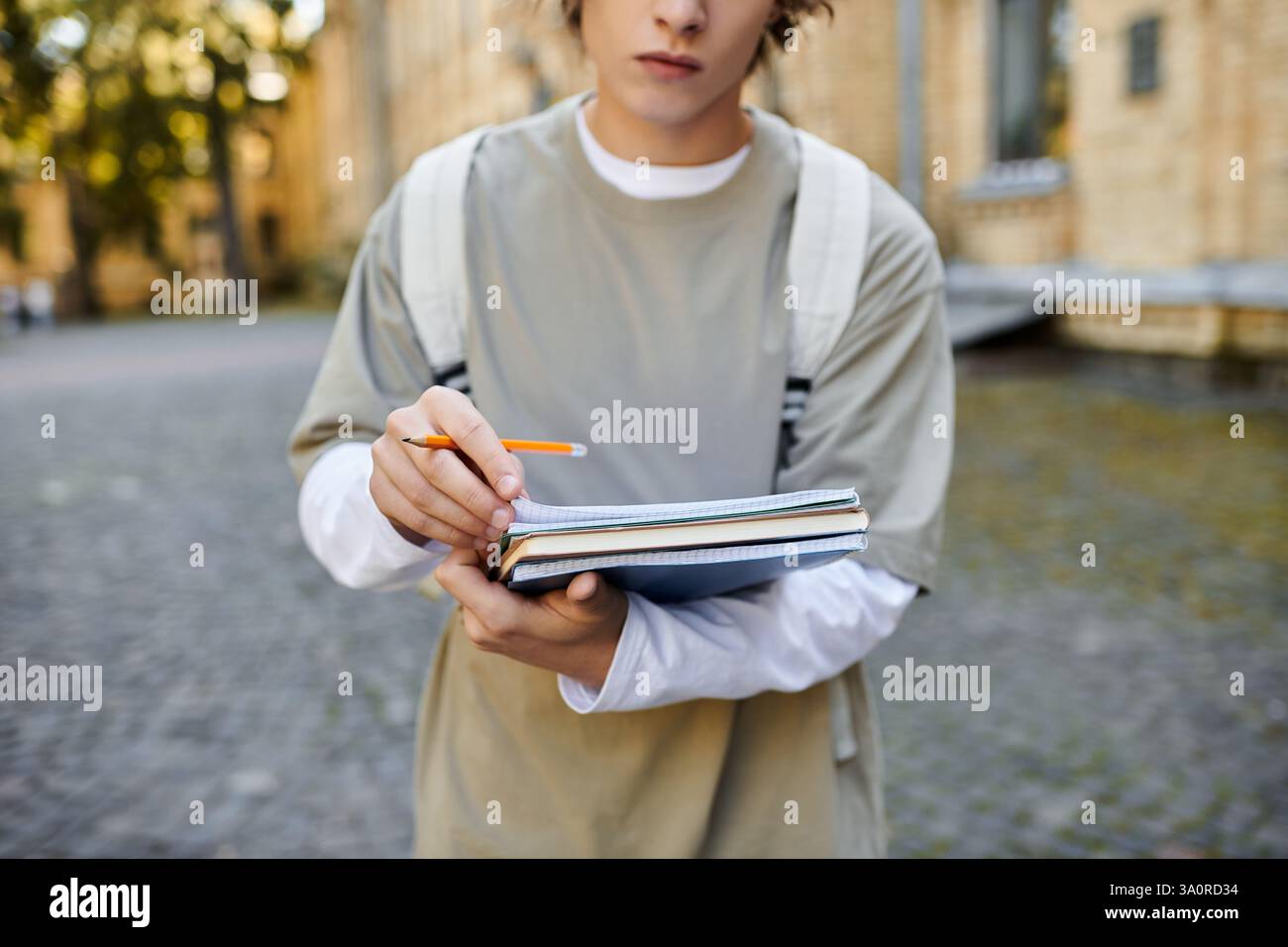 Handsome student engaged in writing with a pencil in a vibrant outdoor ...