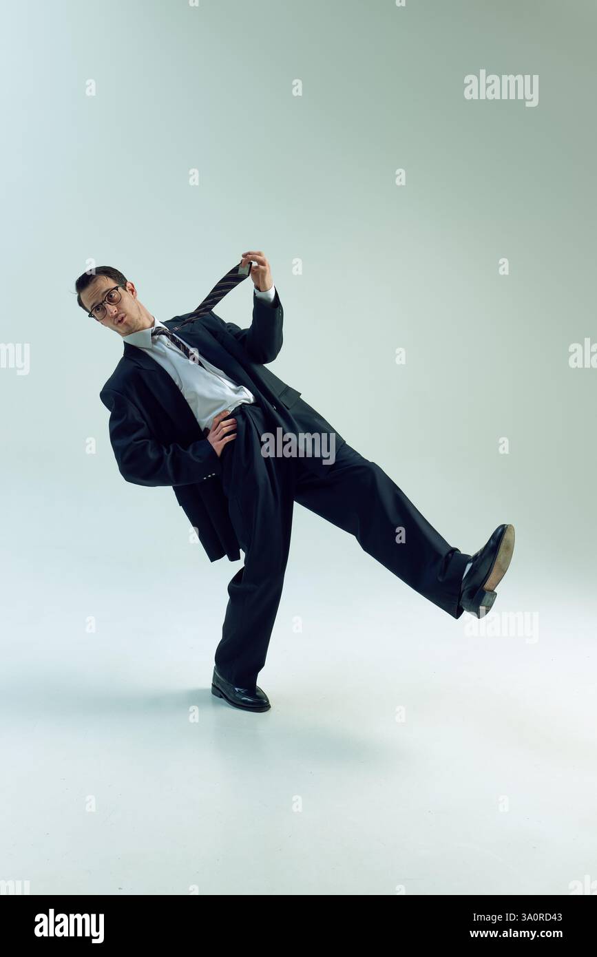 Businessman pulling tie playfully, leaning back, balancing on one leg ...