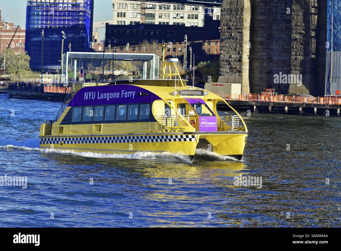 Yellow ferry passing bridge piers on a city river, Manhattan, Brooklyn ...