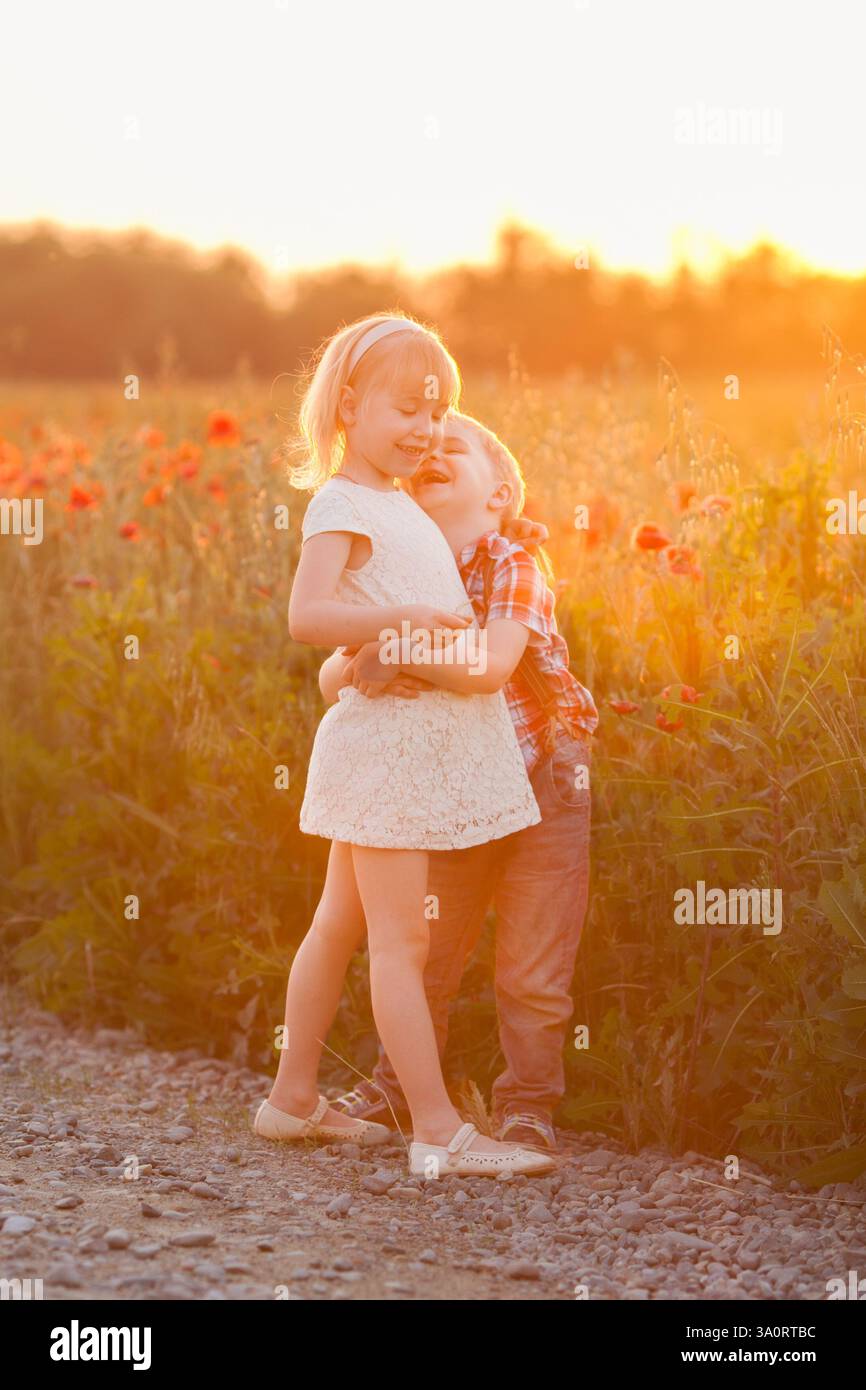 Siblings with blonde hair share a close hug and smile in a poppy field ...