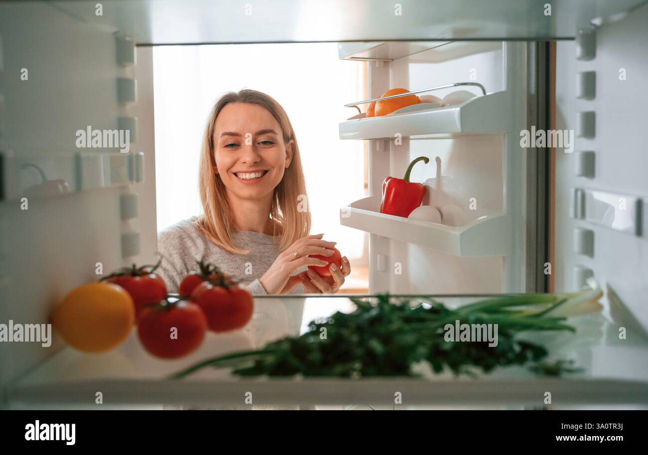 Taking the vegetables from fridge. Beautiful young woman is on the ...