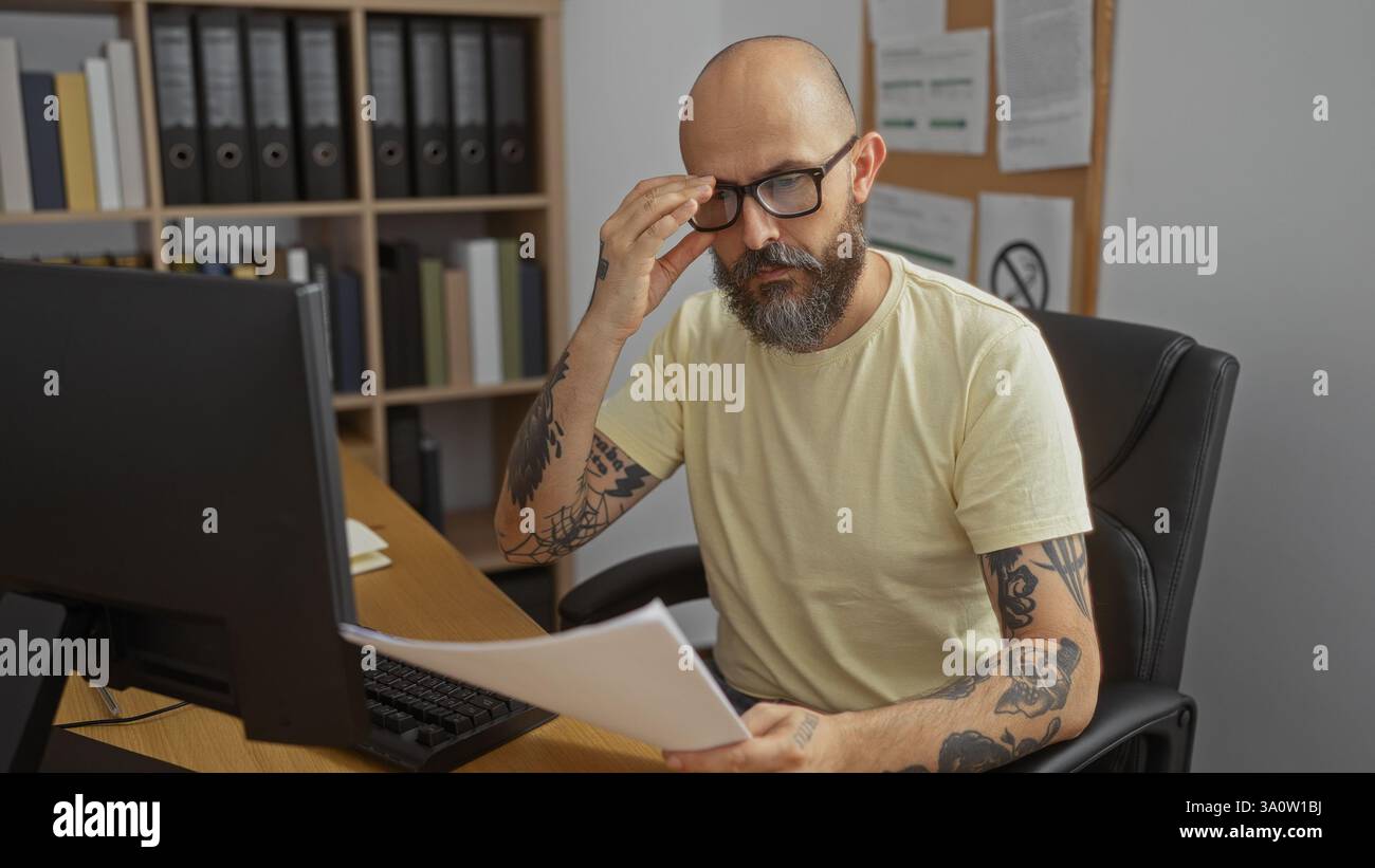 Hispanic man with beard and tattoos working in an office reviewing ...
