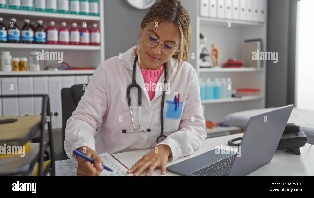 Woman doctor writing at desk in hospital room with laptop and ...