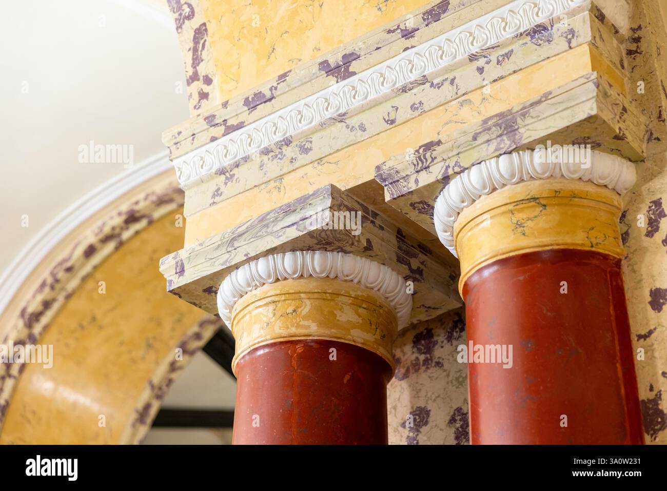 Red stone pillars with yellow white capitals are under ceiling, classic ...