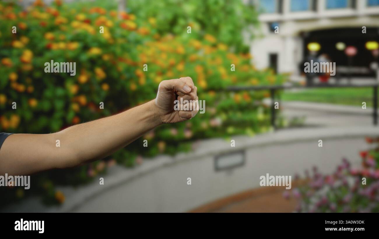 Man's arm extended outdoors with clenched fist against vibrant city ...