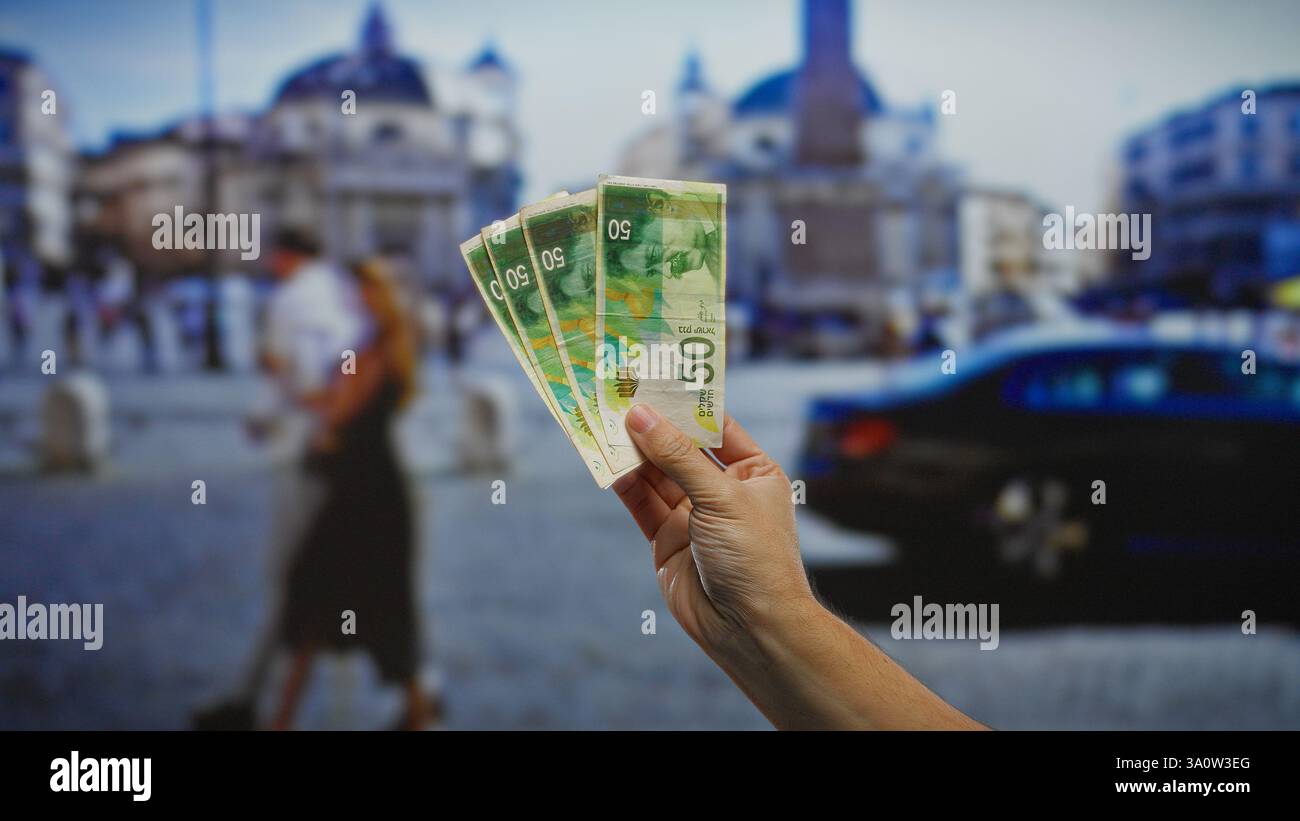 Hand holding israeli shekels in urban street setting, illustrating ...