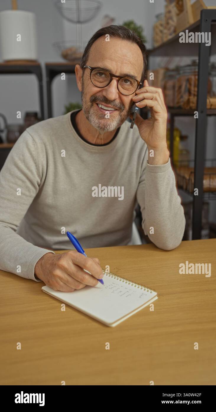 Mature man talking on phone while writing notes in office setting ...