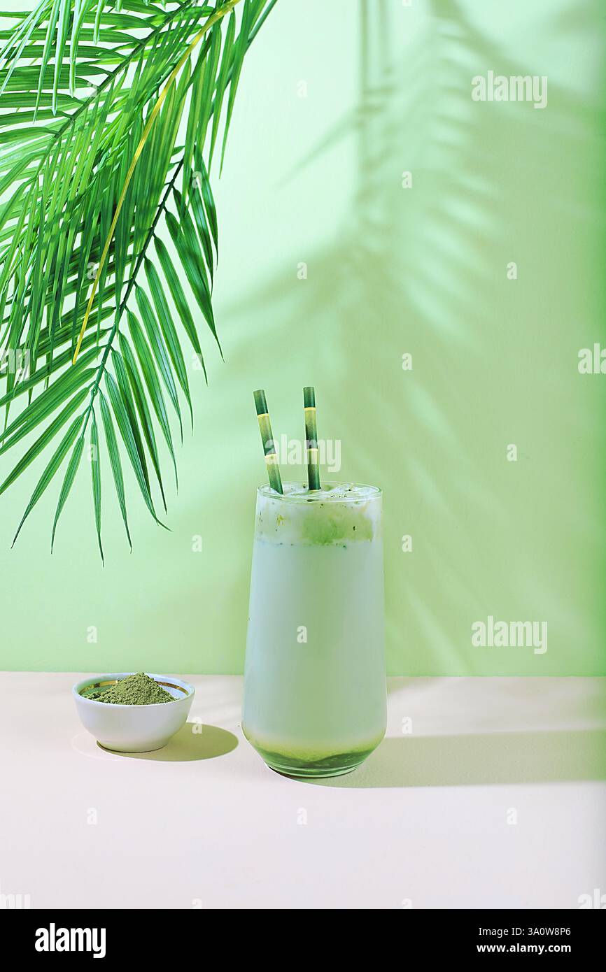 Green tea matcha latte in a glass with bamboo tubes on a modern light ...