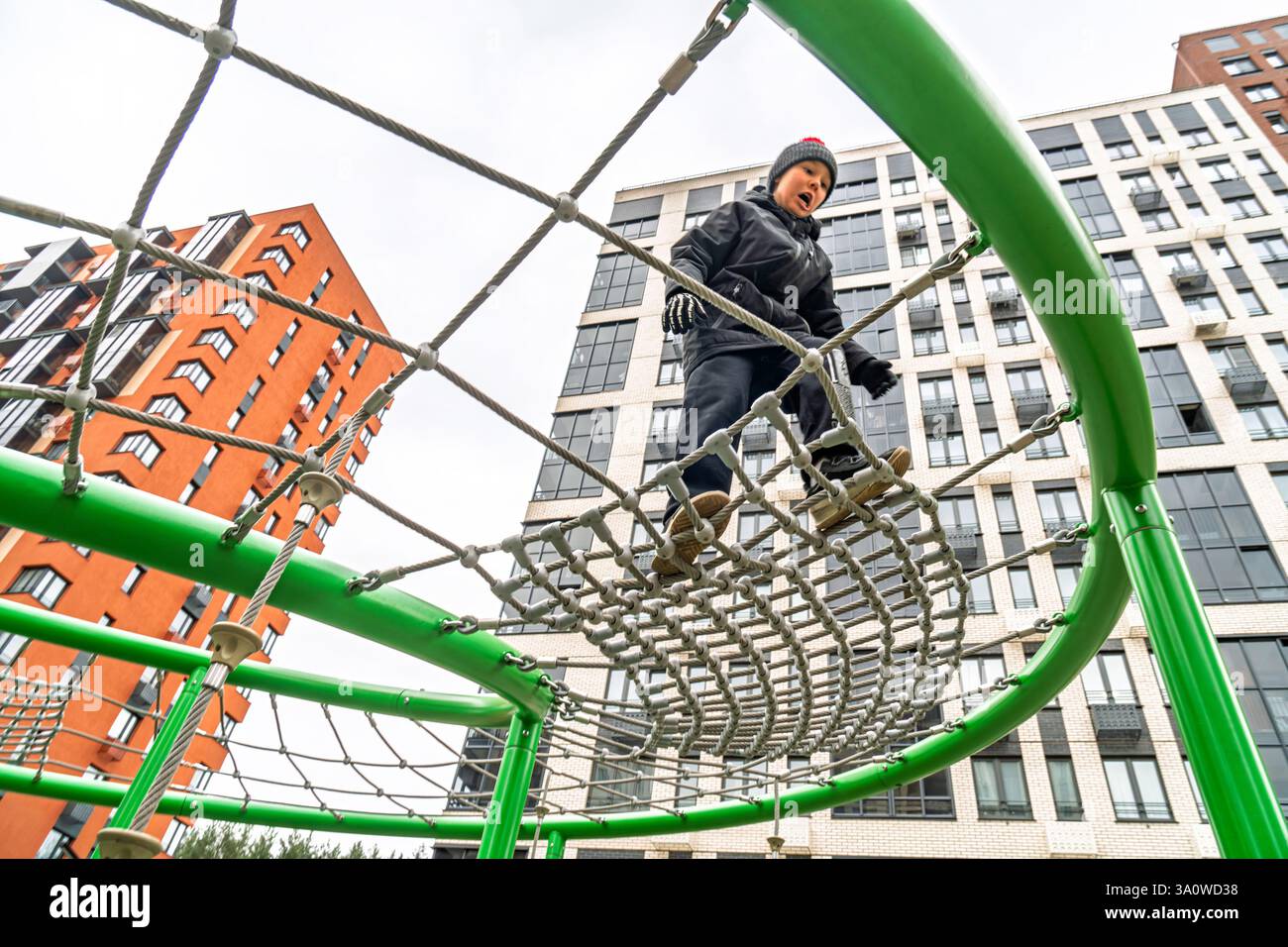 A child in warm clothes climbing a rope net on a playground surrounded ...