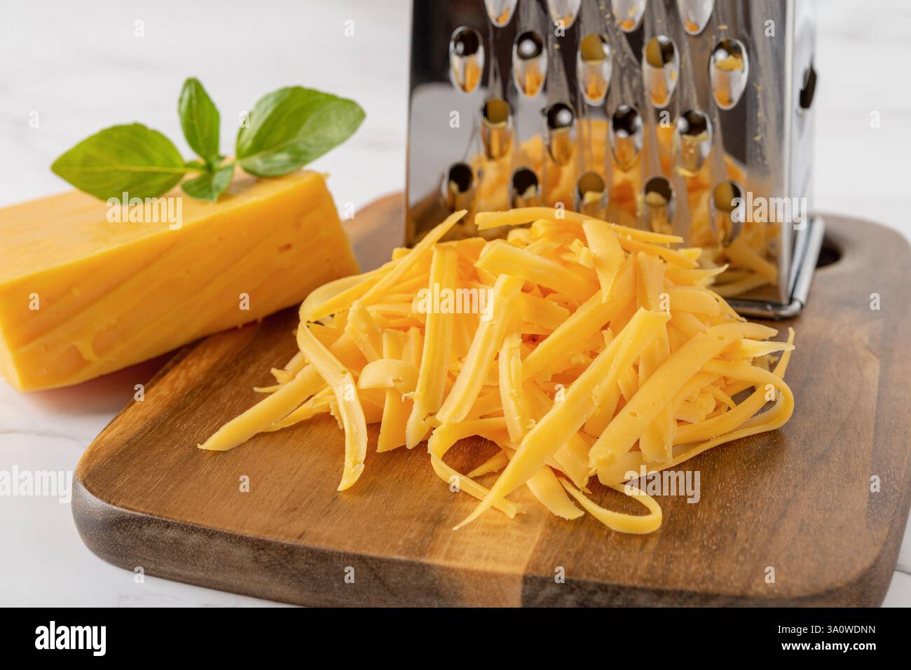 Whole and grated cheddar cheese close-up. Shredded orange cheese and metal grater on a wooden ...