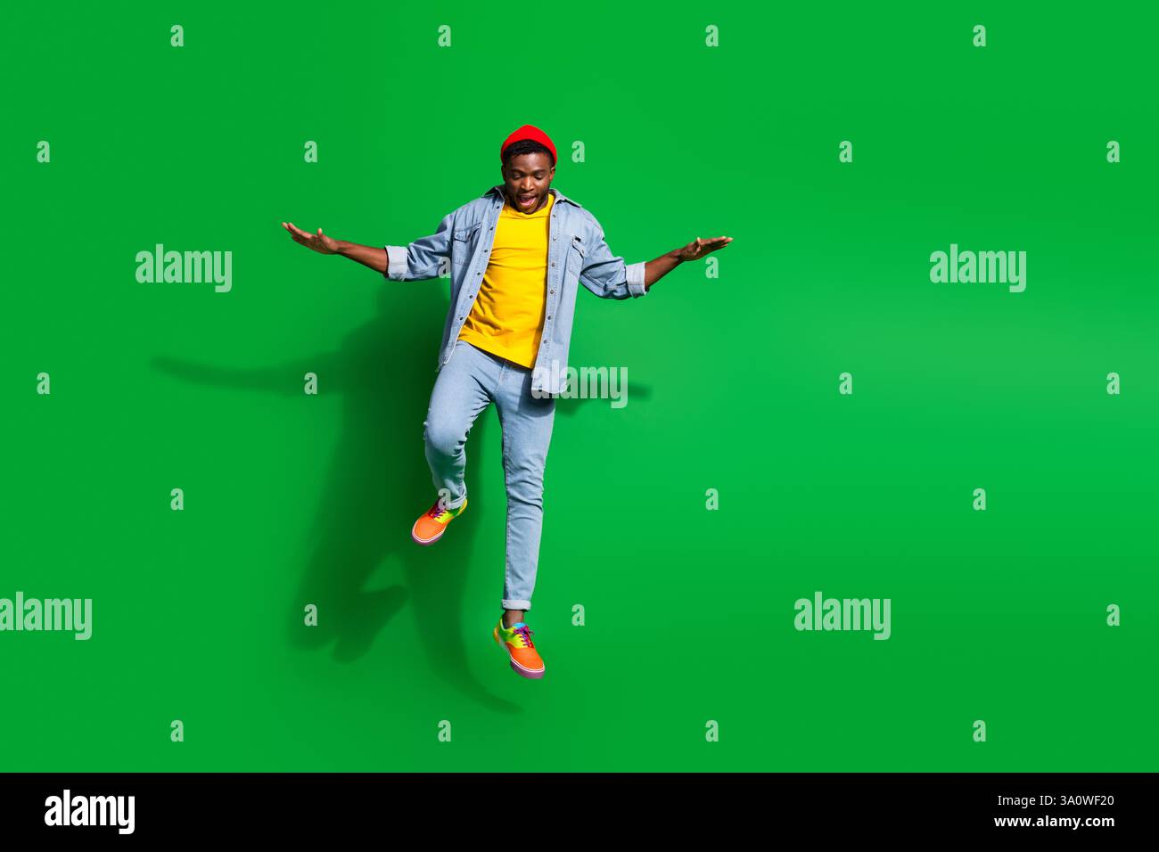 Stylish young man jumping cheerfully against a vibrant green background ...