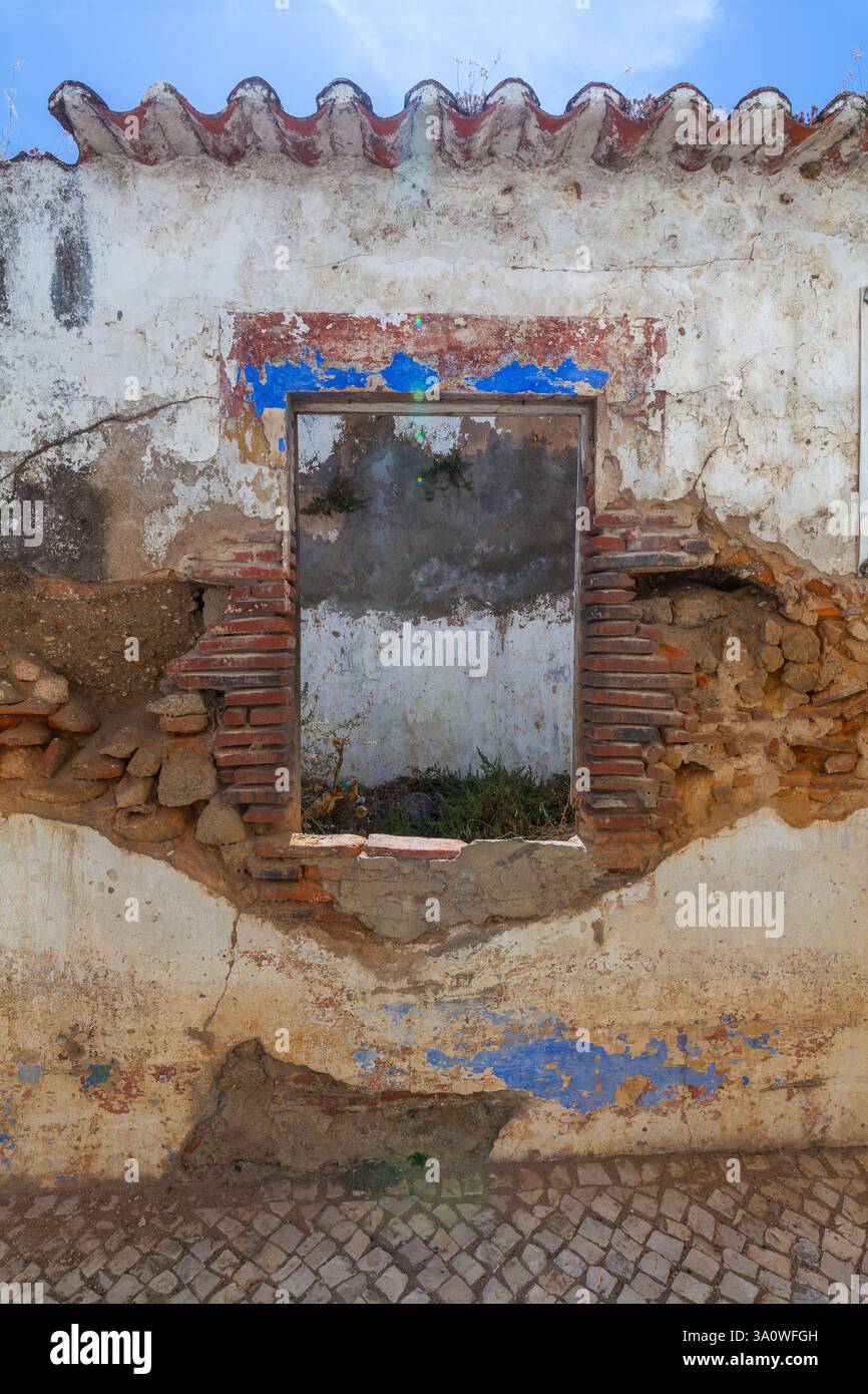 A weathered, abandoned wall with a partially crumbled window frame and ...