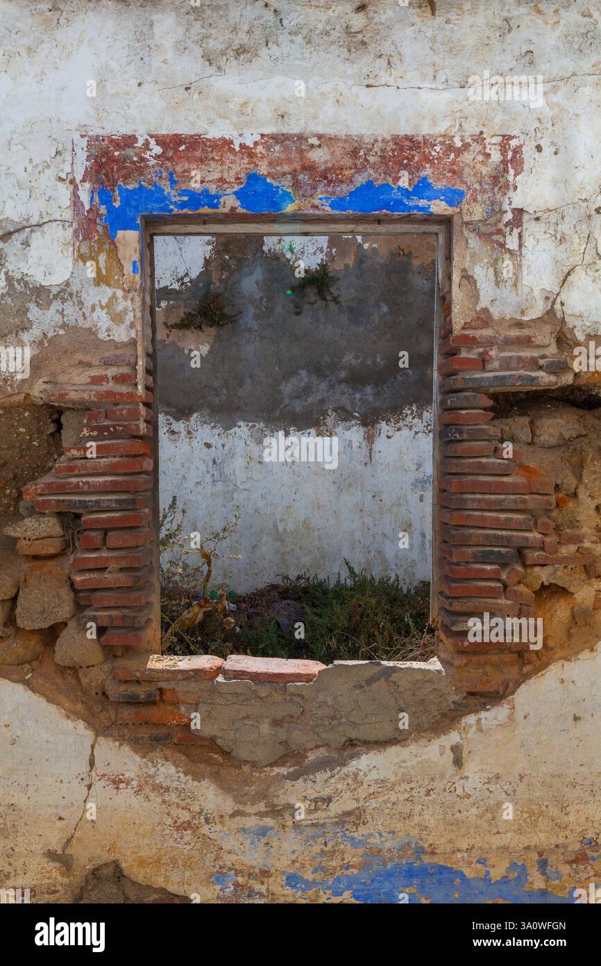 A weathered, abandoned wall with a partially crumbled window frame and ...