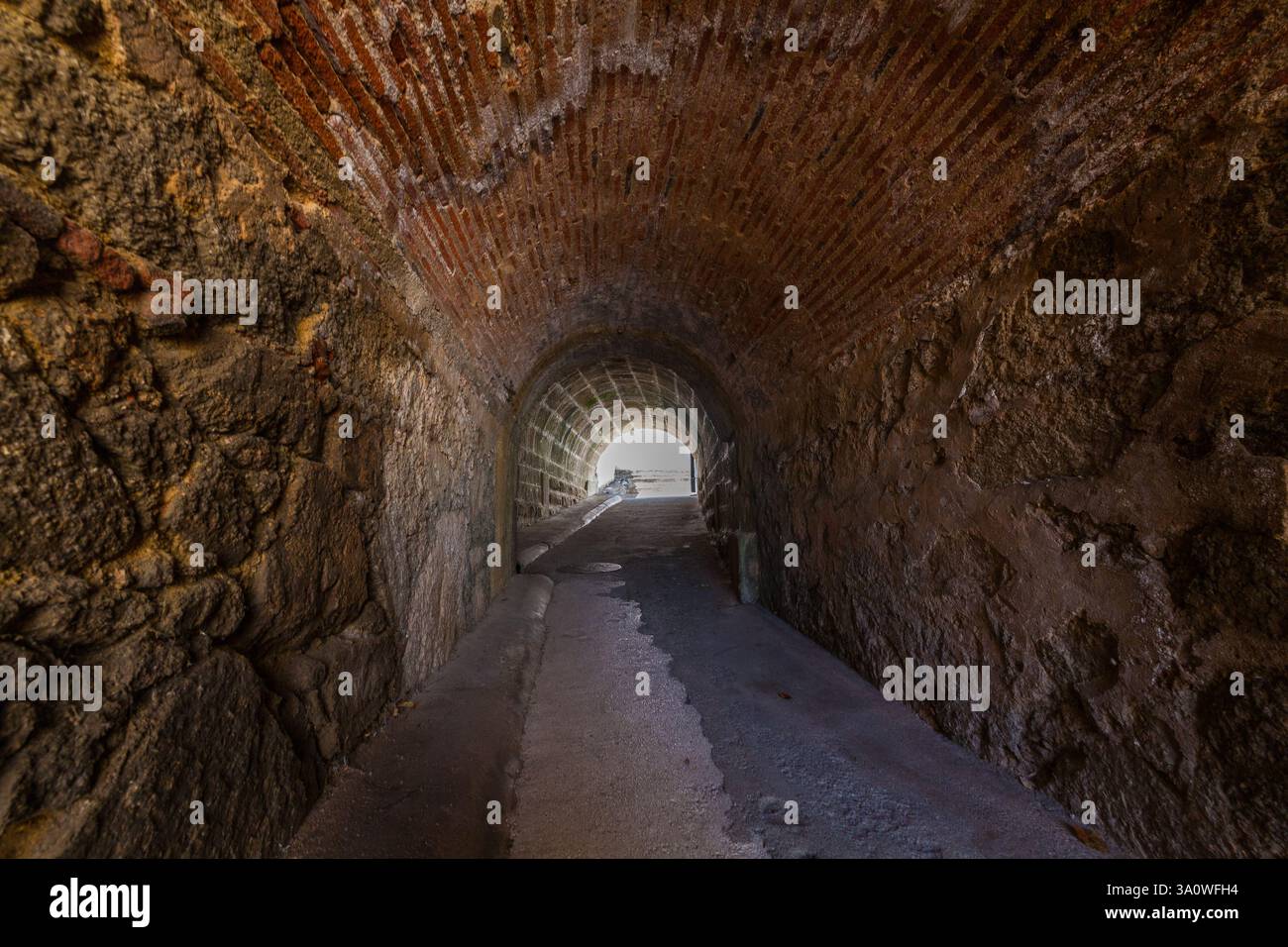 An arched brick tunnel with textured, aged walls leading towards an ...