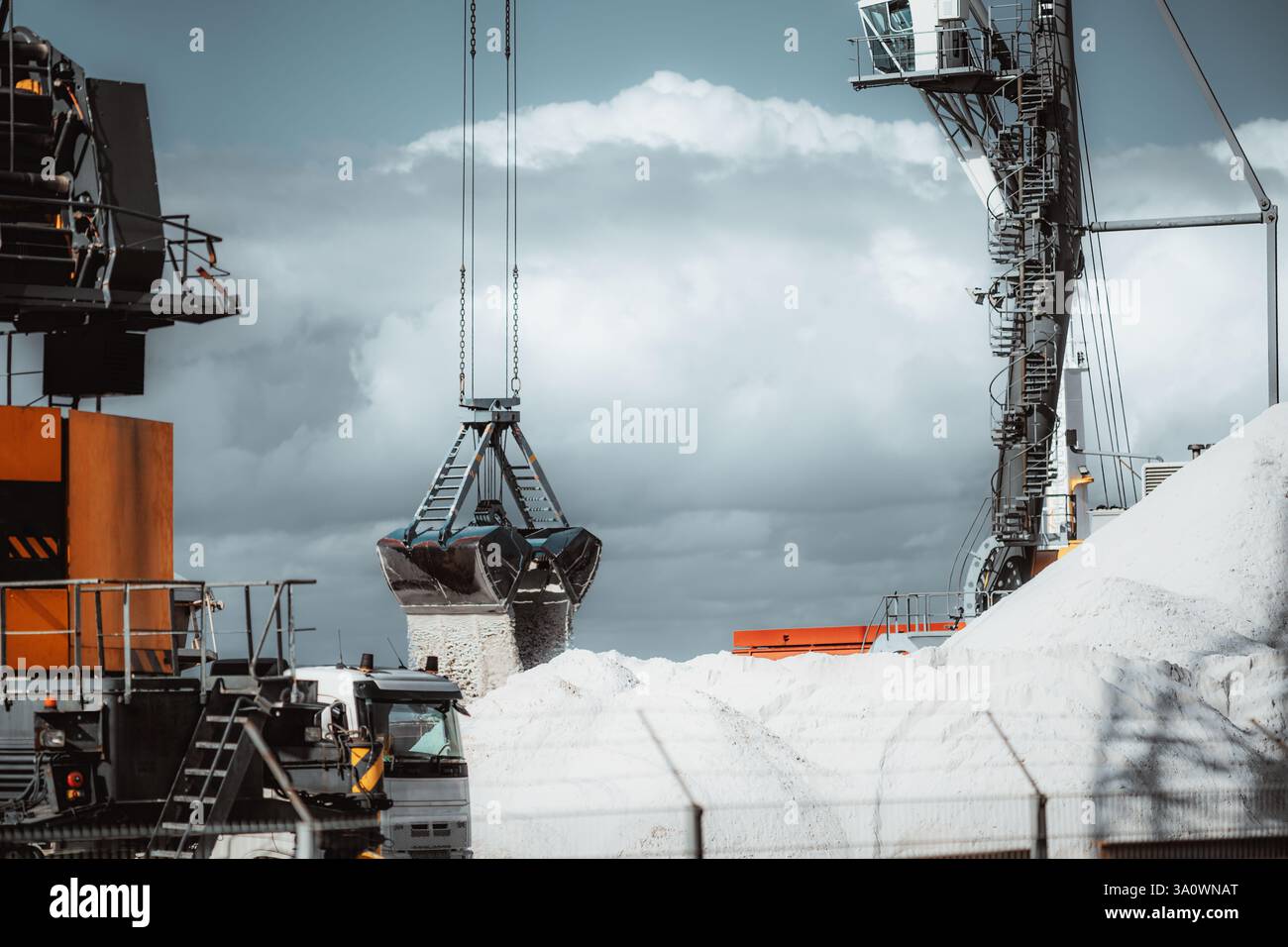 A telephoto shot of a large industrial grab crane unloads bulk material ...