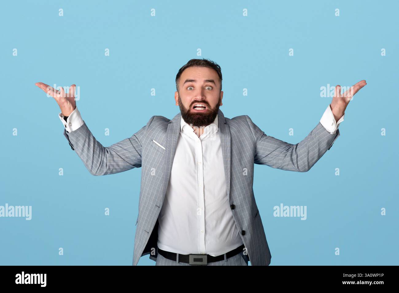 Emotional millennial office worker shrugging his shoulders against blue ...