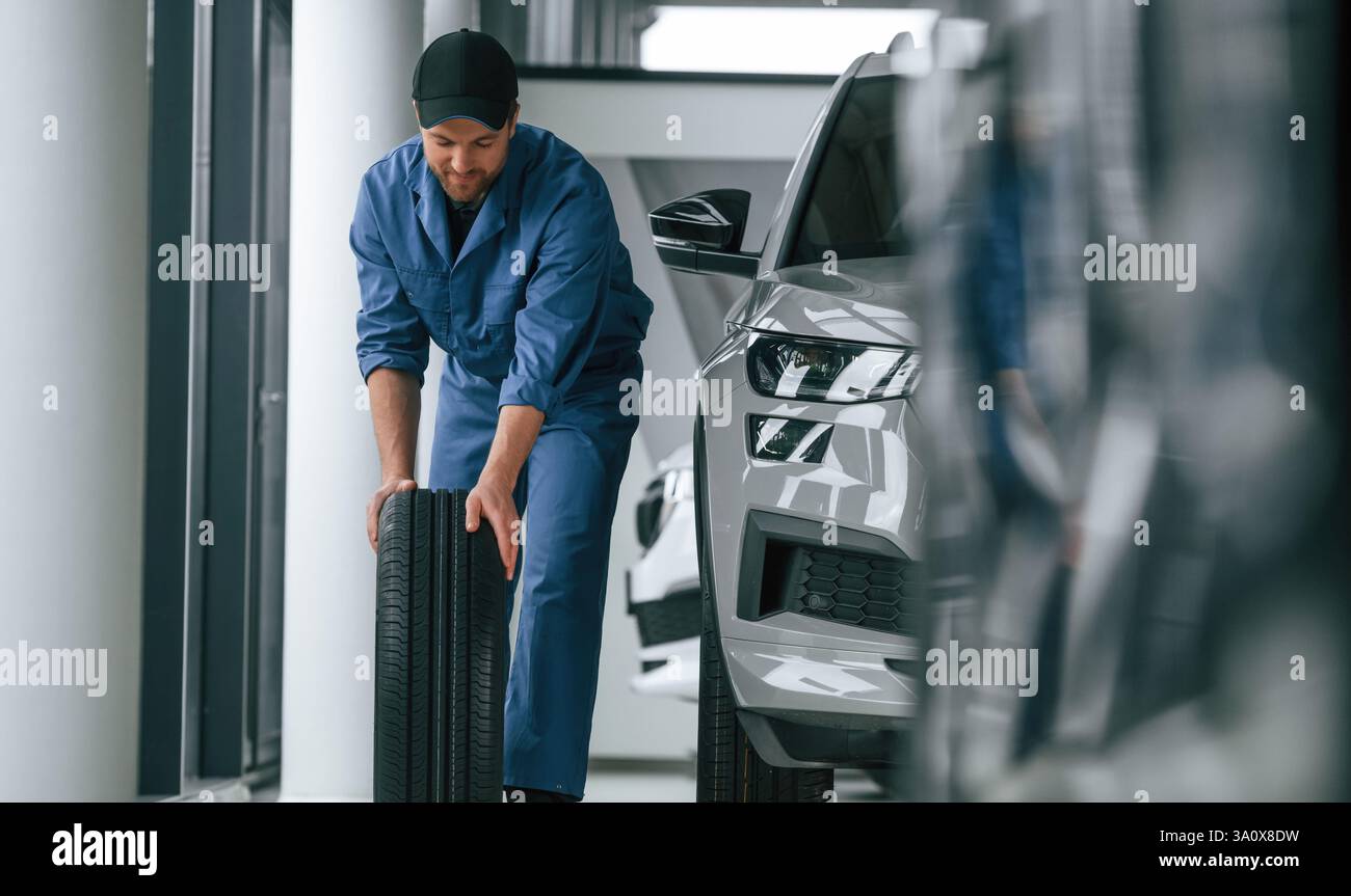 Moving the tire. Man in blue uniform is working in the car service ...