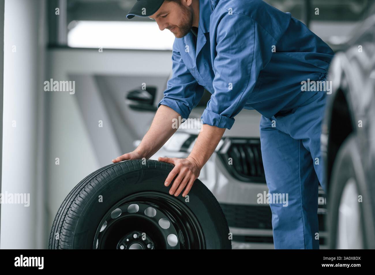 Moving the tire. Man in blue uniform is working in the car service ...