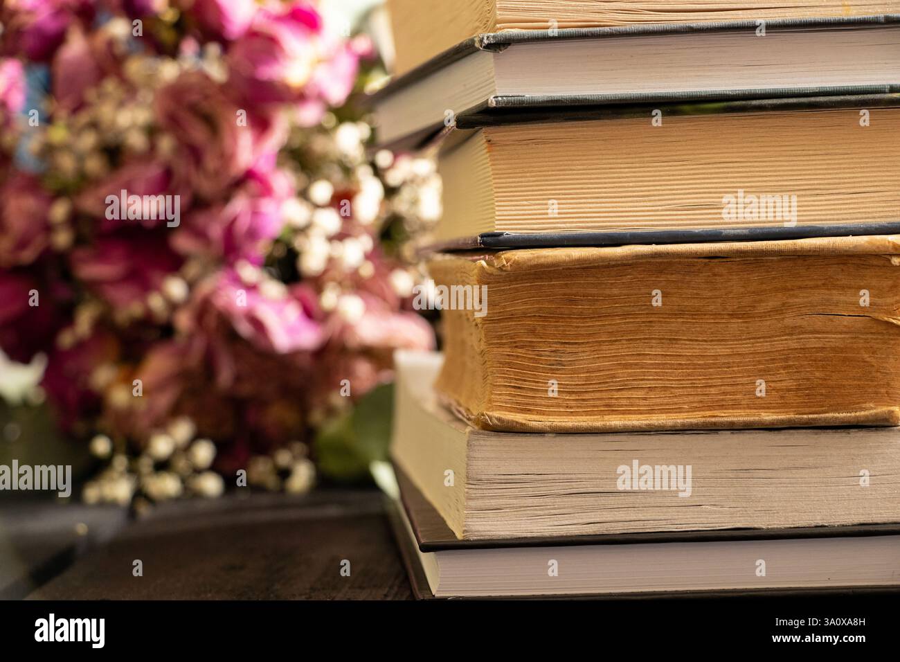 Stack of books on wooden table at home and bouquet of dried roses ...