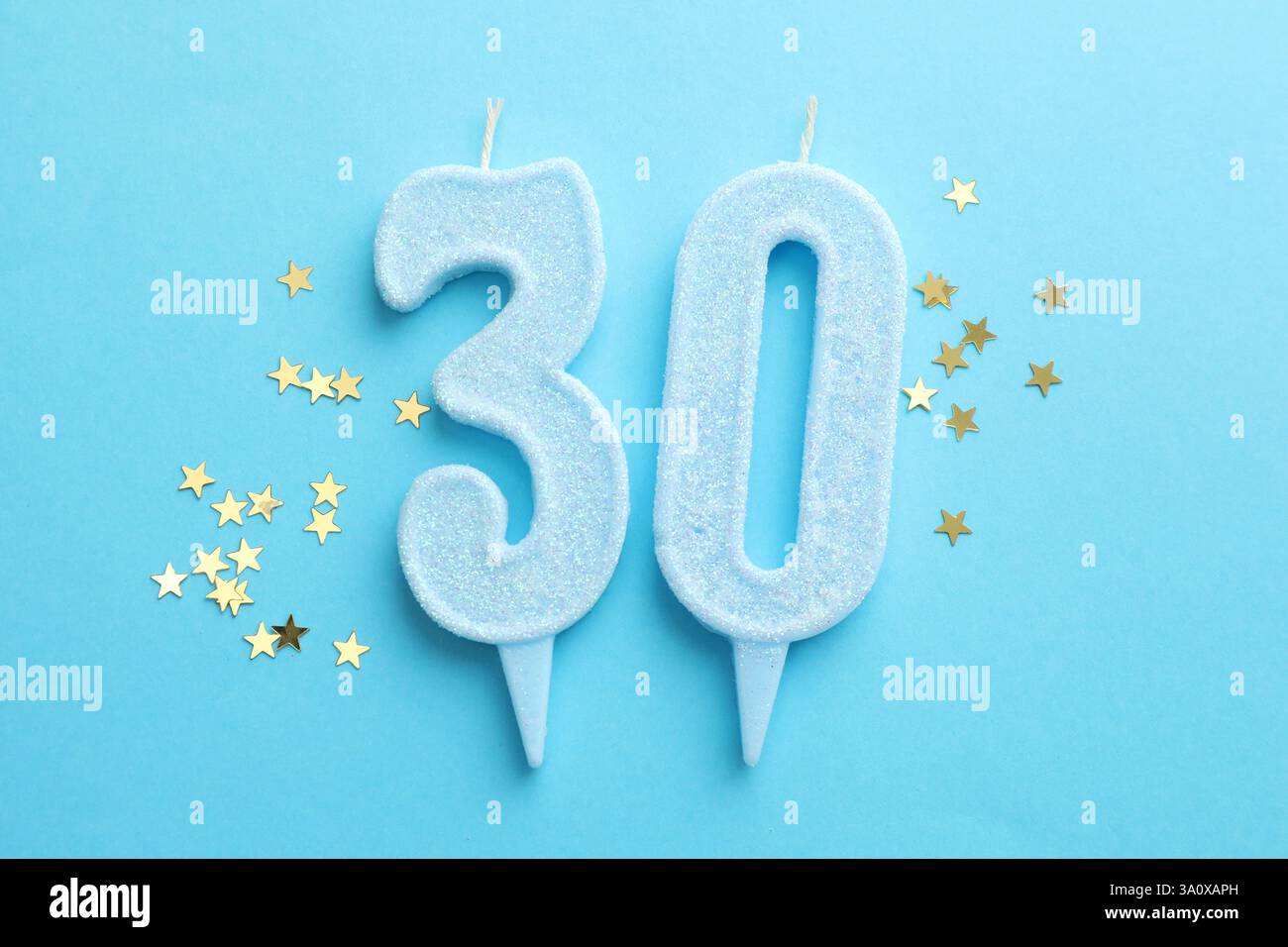 30th birthday. Number shaped candles and confetti on light blue ...