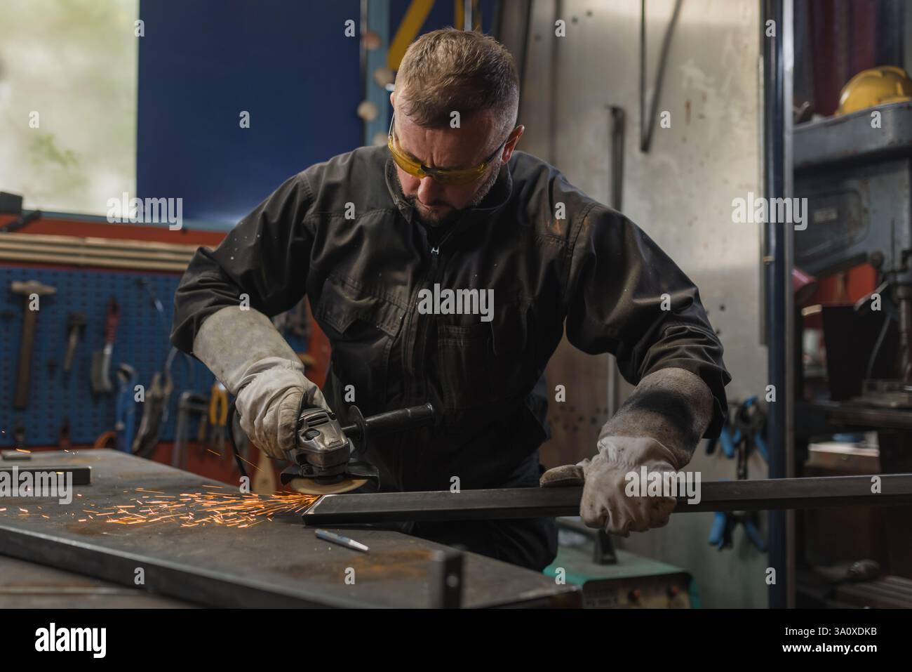 Skilled manual worker wearing protective equipment grinding steel in a ...