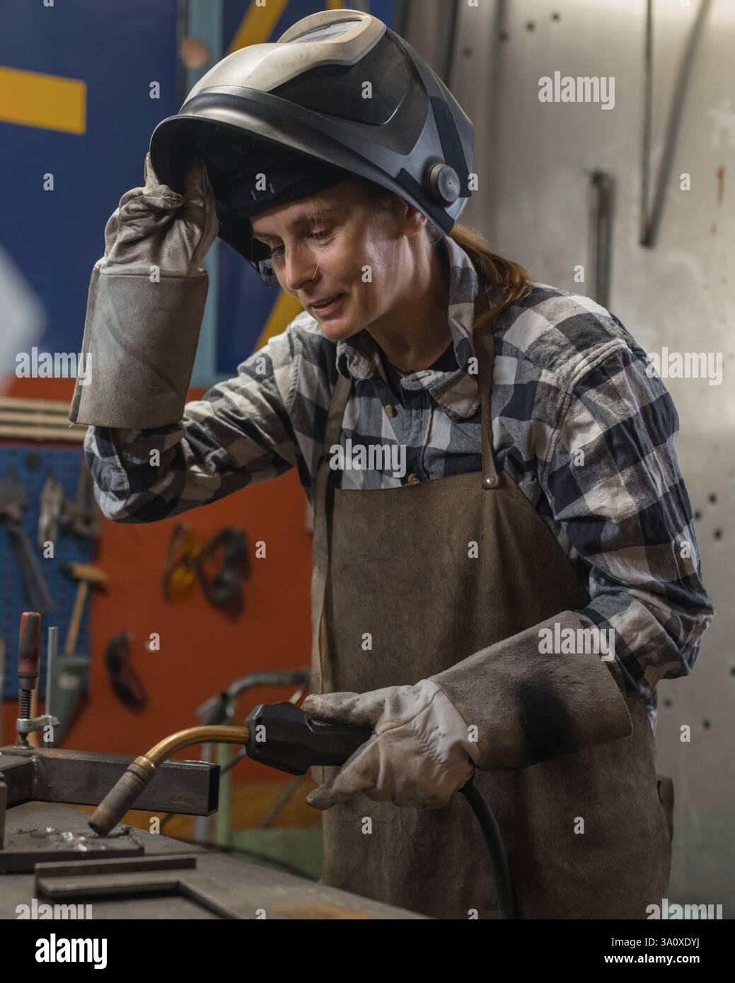 Female welder using a welding torch, taking off the face shield to look ...