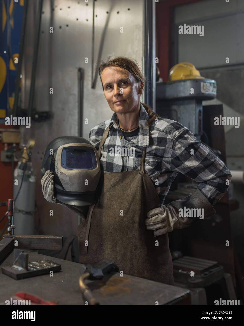 Female welder using a welding torch, taking off the face shield to look ...