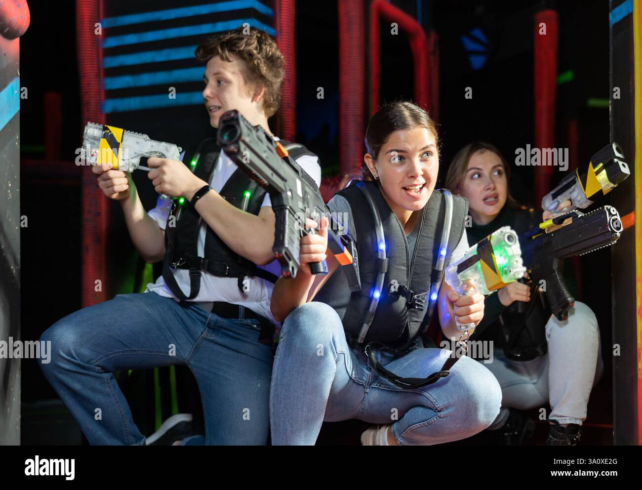 Three people having fun playing lasertag ducking behind cover in arena ...