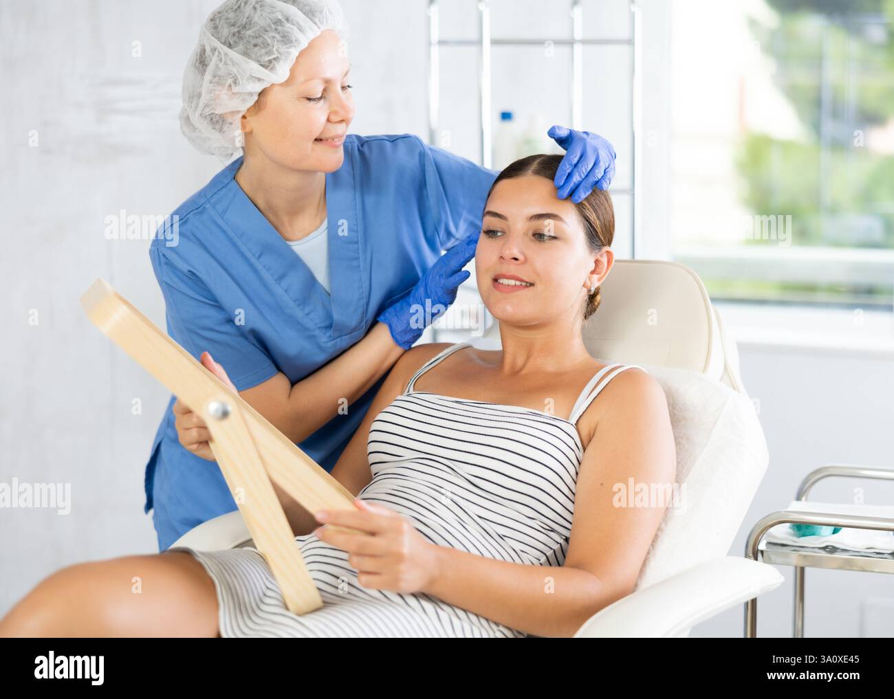 Woman cosmetologist examines patients forehead after lifting procedure ...