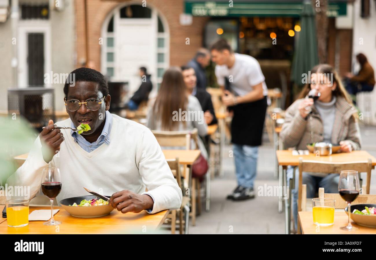 On open area of cafe, African man in restaurant eating salad Stock ...