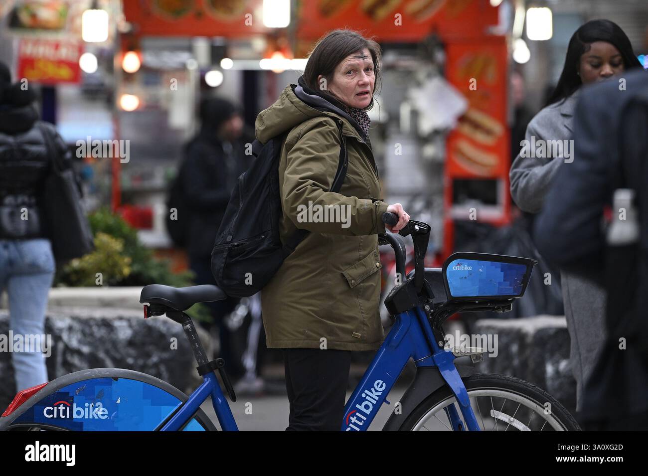 A woman on a bicycle is marked with a cross of black ash on her ...