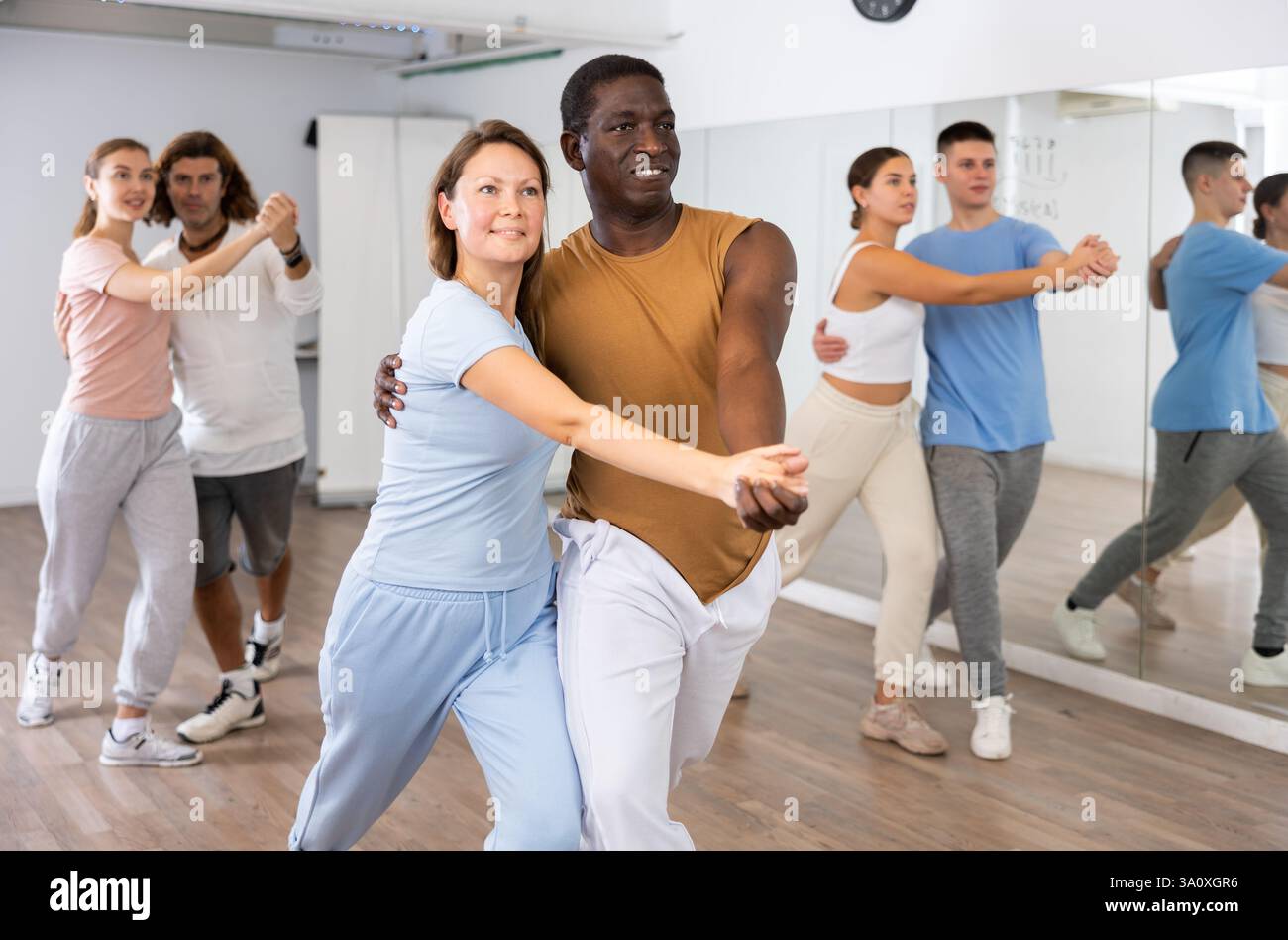 Smiling dancing people practicing movements while dancing in pairs in ...