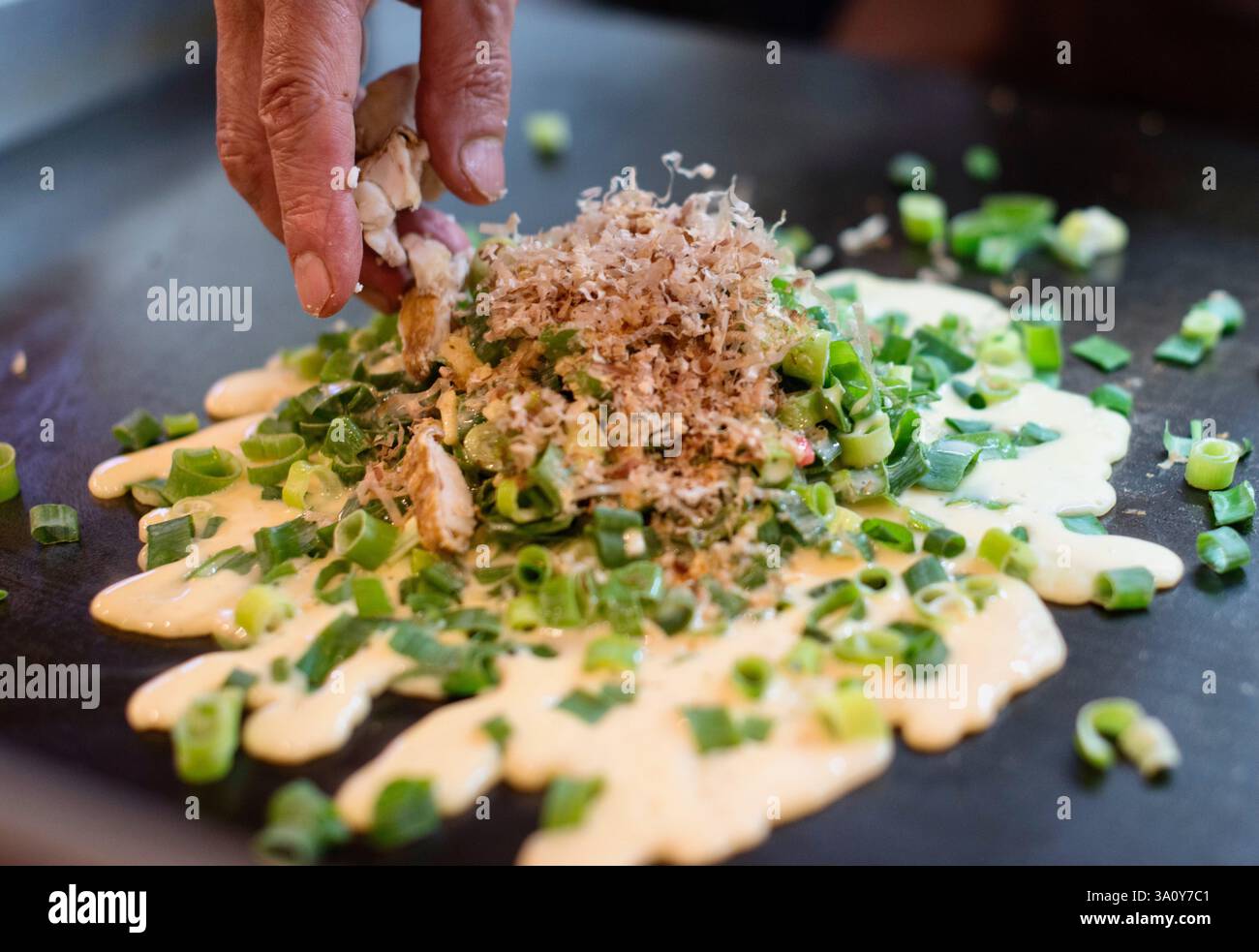 Chef Masanobu Nishikura sprinkles toppings on the top of a sizzling ...