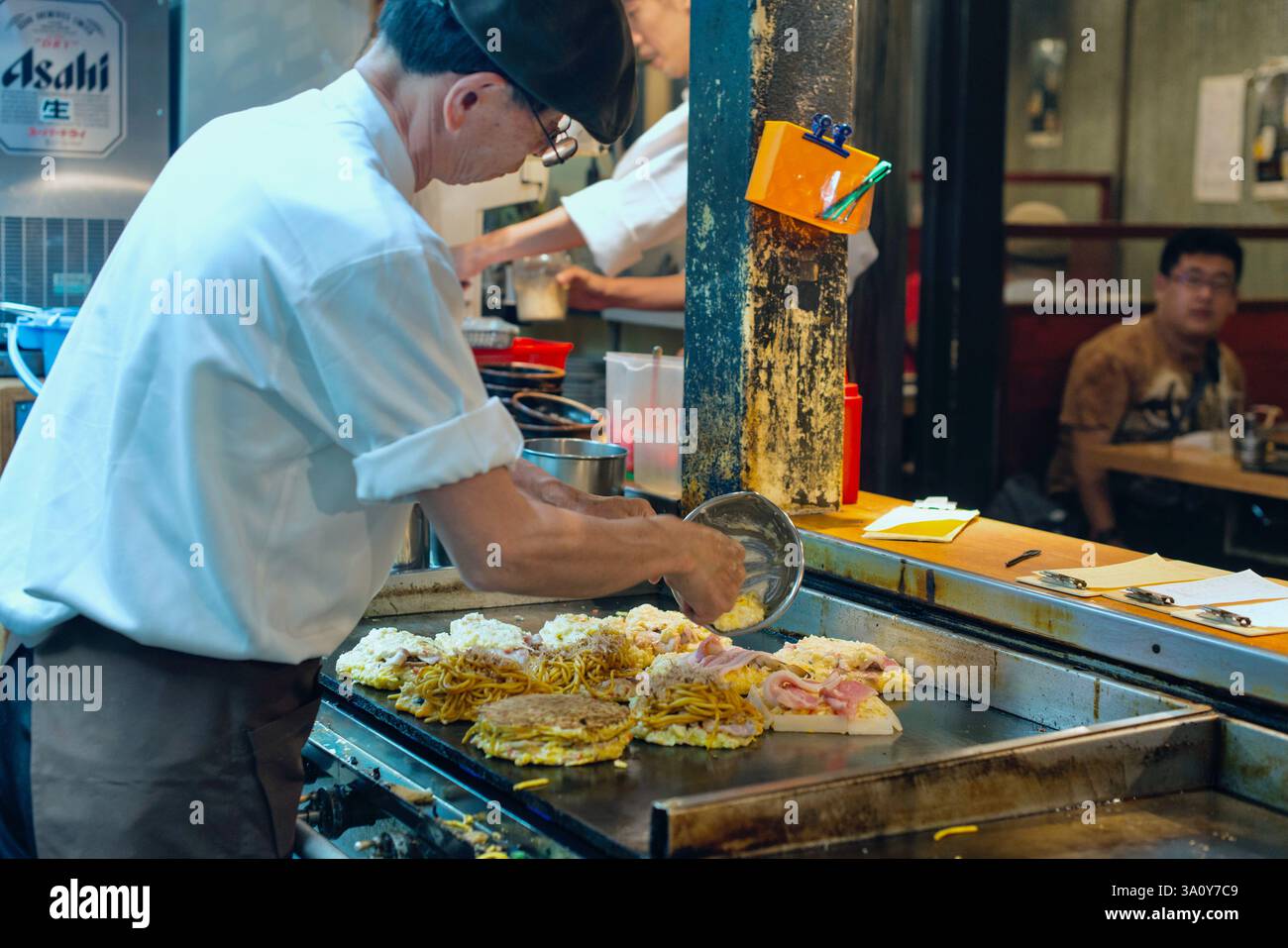Chef Masanobu Nishikura spoons out the batter onto the griddle as he ...