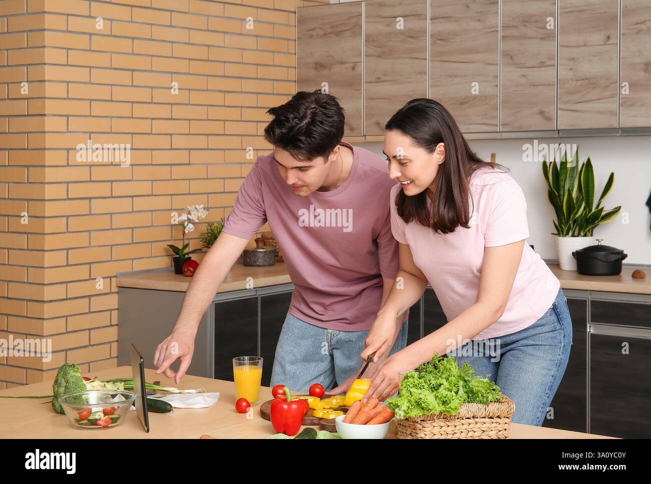 Happy young couple watching tutorial together while cooking in kitchen ...