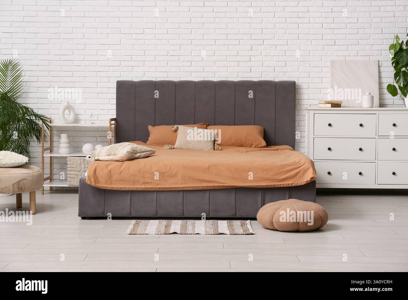 Comfortable bed with pillows, shelving unit, chest of drawers and pouf ...