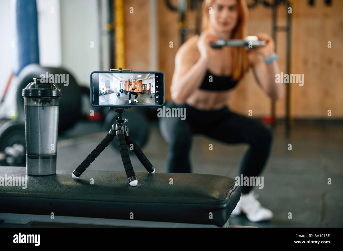 Doing squats, shooting video by smartphone. Beautiful strong woman is ...