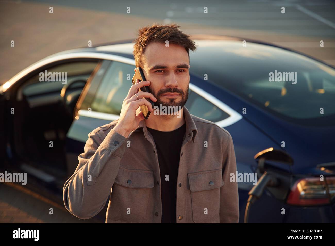 Having a call while automobile is charging. Man is standing near his ...